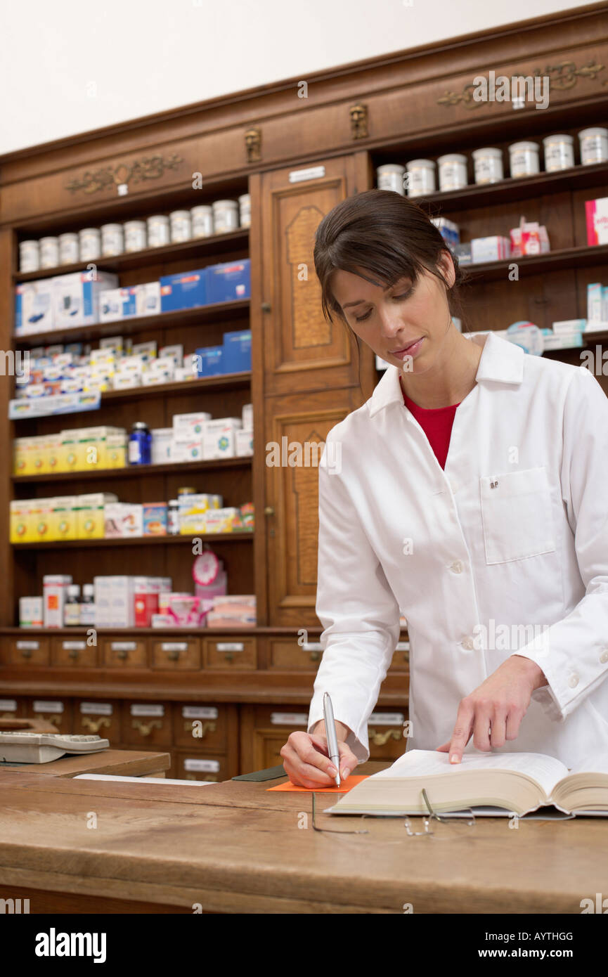 Female pharmacist reading a book while making notes Stock Photo - Alamy
