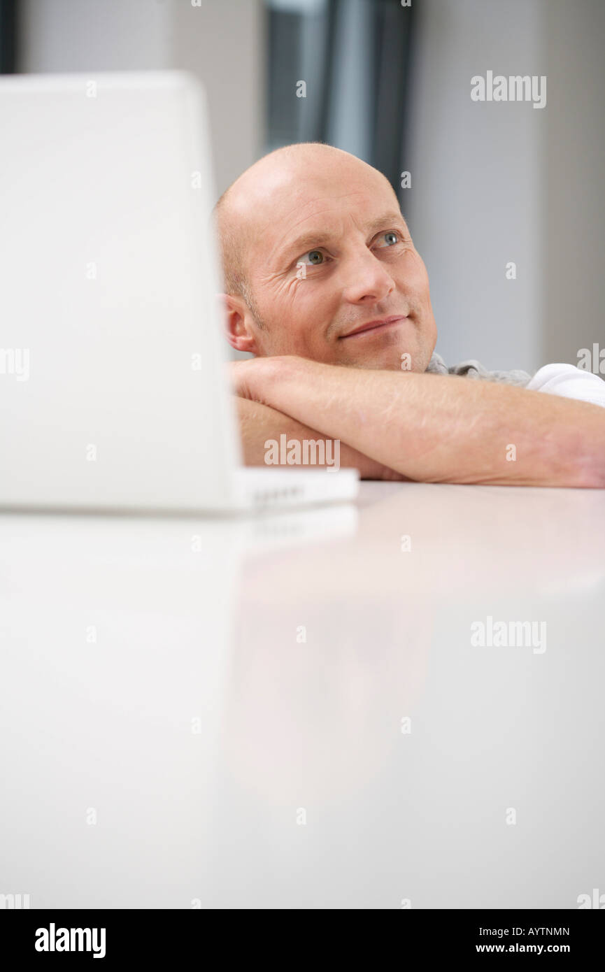 Mature man crouching at a table with a laptop Stock Photo - Alamy