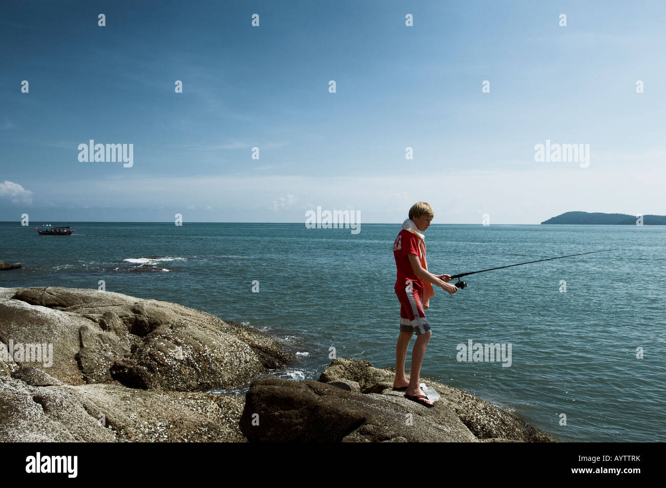Boy fishing from rocks Stock Photo - Alamy