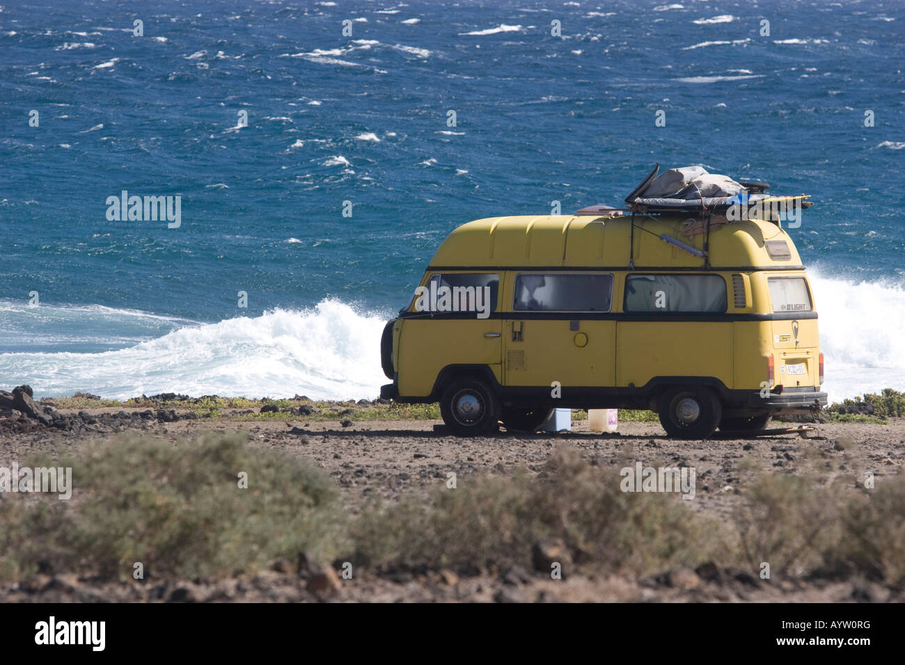 Yellow VW camper van parked on cliff overlooking sea with surf board on ...