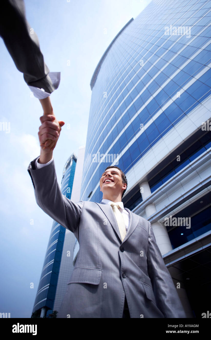 man shaking hands in front of building at low angle Stock Photo - Alamy