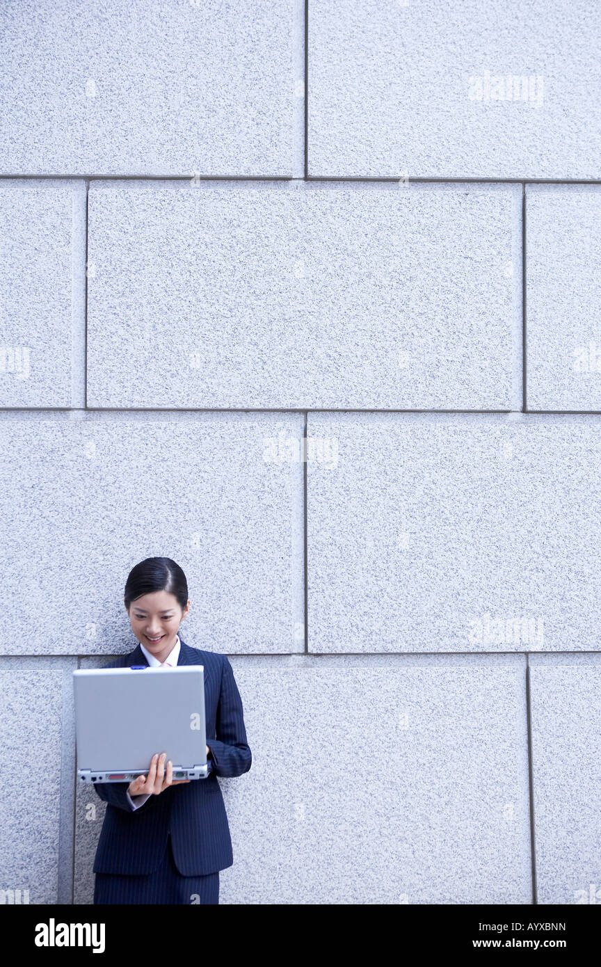 a woman using laptop computer with leaning over wall Stock Photo - Alamy