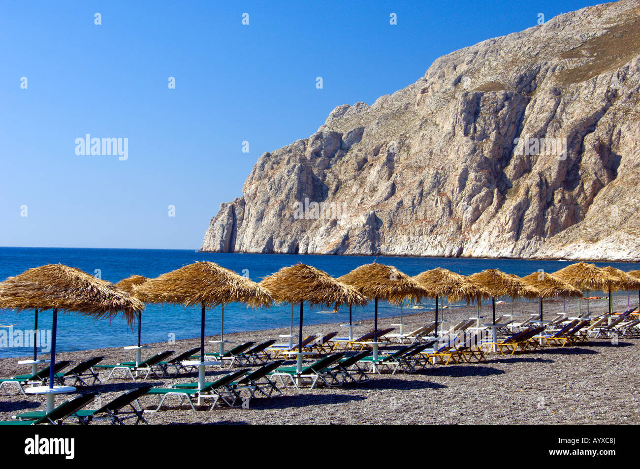 The black sand beaches with umbrellas and lounge chairs in Kamari on ...
