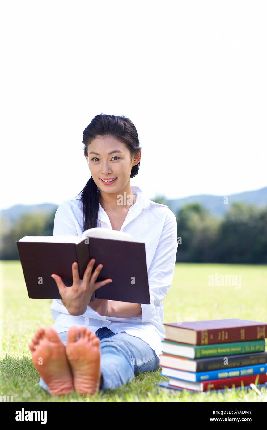 a barefooted woman reading a book with sitting on the grass field Stock ...