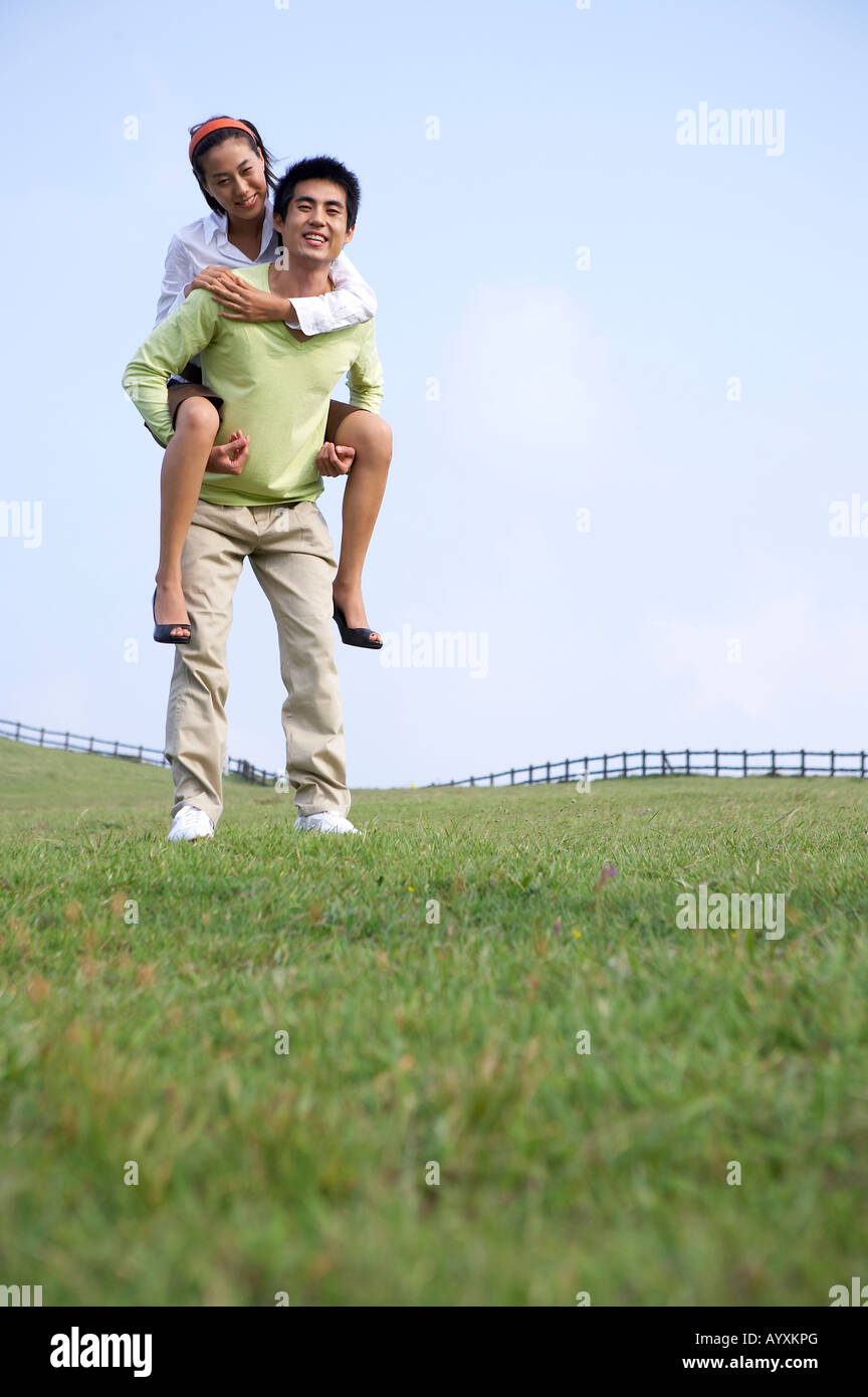 a man carring her on his back and a woman in the grass field Stock ...