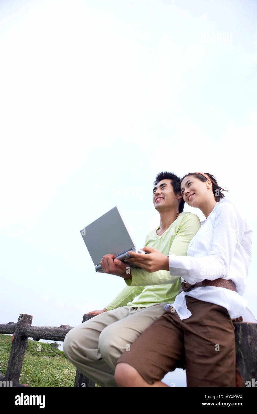 a couple usning laptop computer sitting on wood fence Stock Photo - Alamy