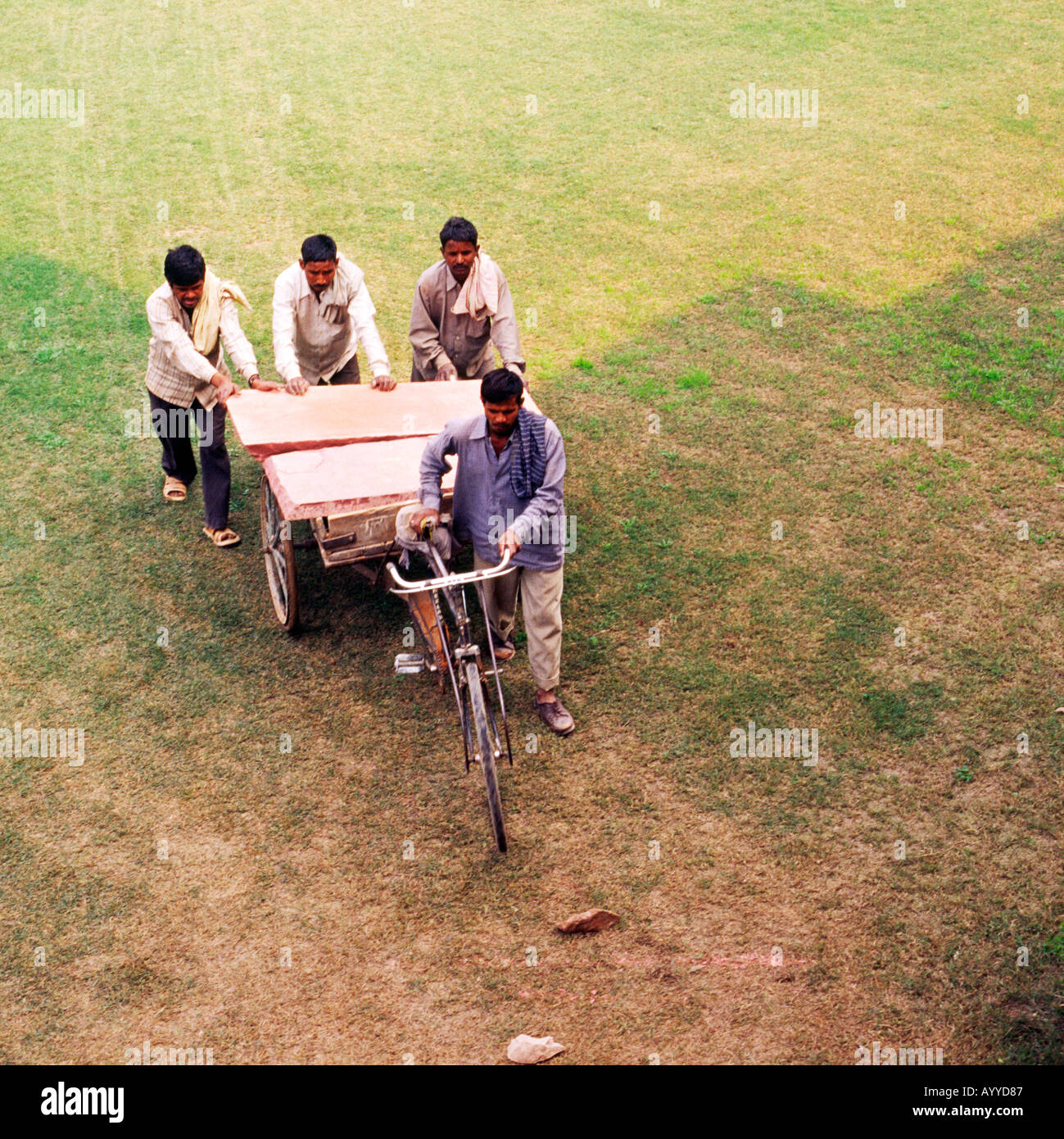 Four Indian men pushing a cycle rickshaw across the grass yard with ...