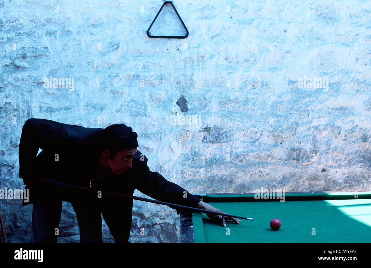 One unrecognizable male in the shade playing pool on an outdoor game ...