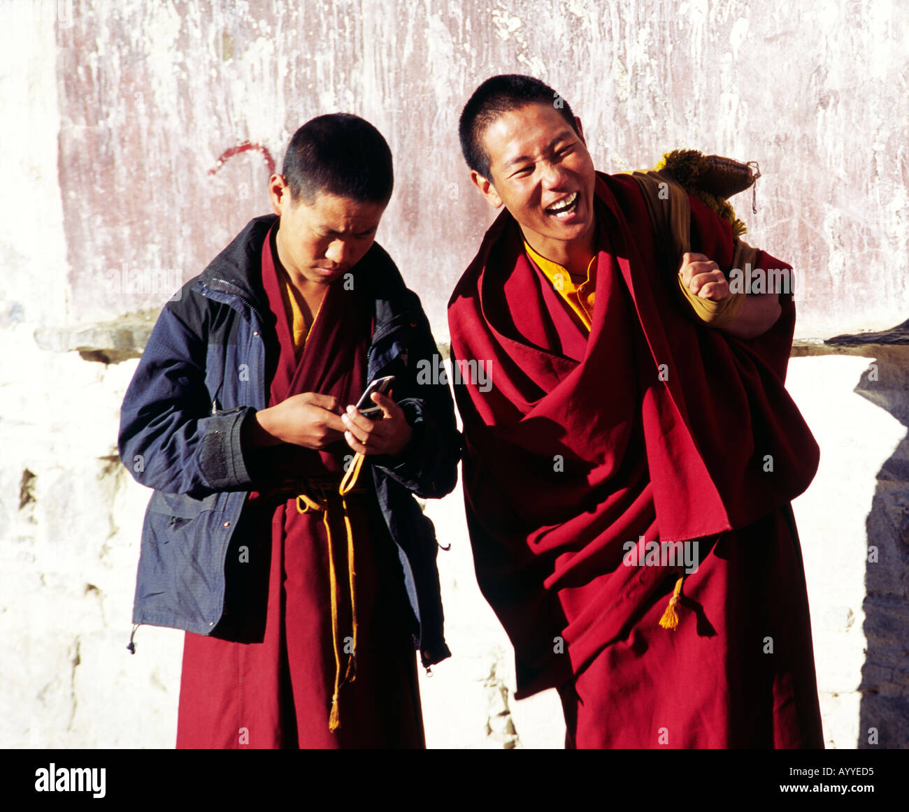 Two Tibetan Buddhist monks wearing red robe standing laughing and ...