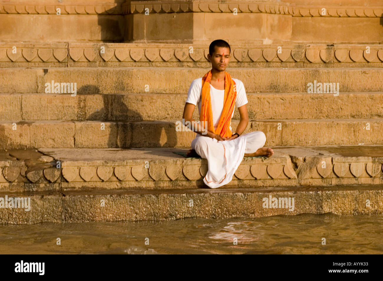 Young Indian priest praying and meditating at ghat on the bank of ...