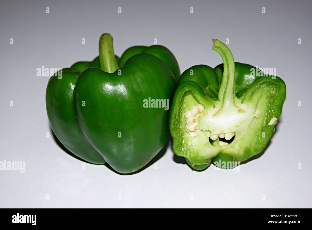 Green bell pepper (capsicum annuum) cut in half on a plain background ...
