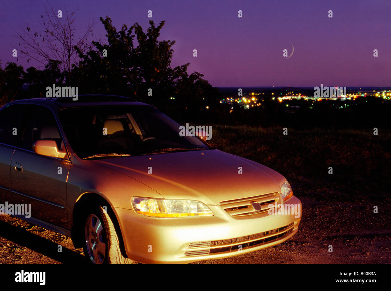 A car sitting atop a city overlook at twilight with a crescent moon ...