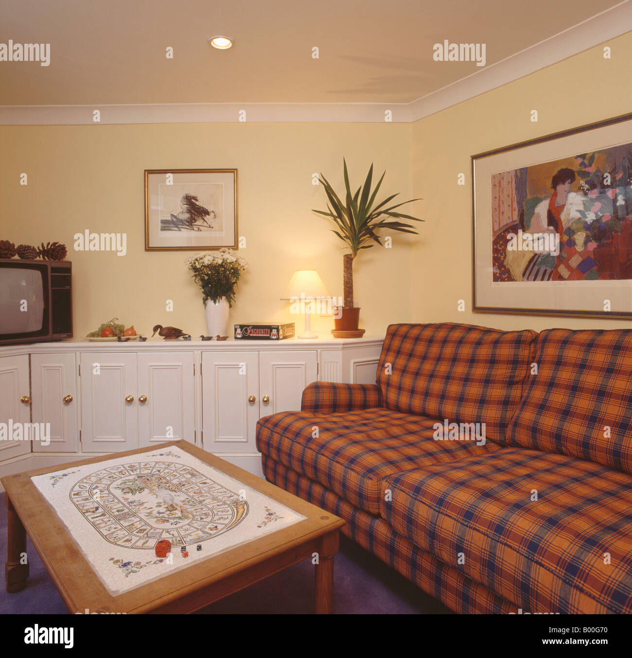 Orange and blue checked sofa in pastel yellow living room with fitted ...