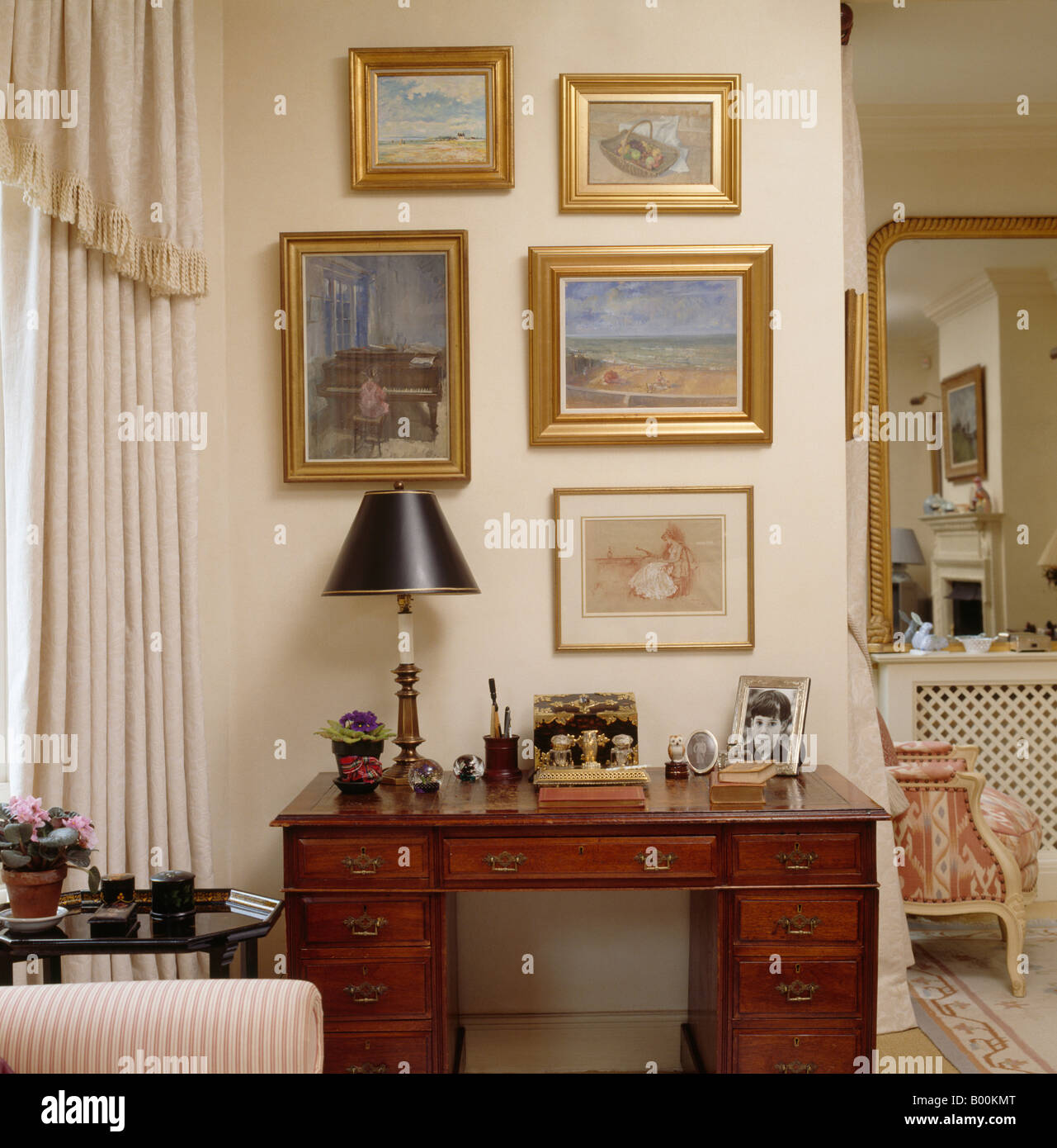 Collection of pictures above lamp on antique desk in traditional cream ...