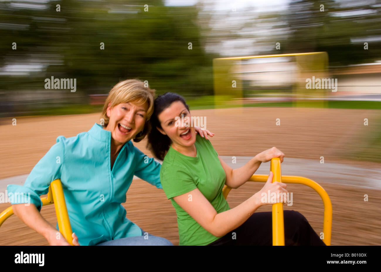 Mother and daughter or good friends having fun in playground spinning ...