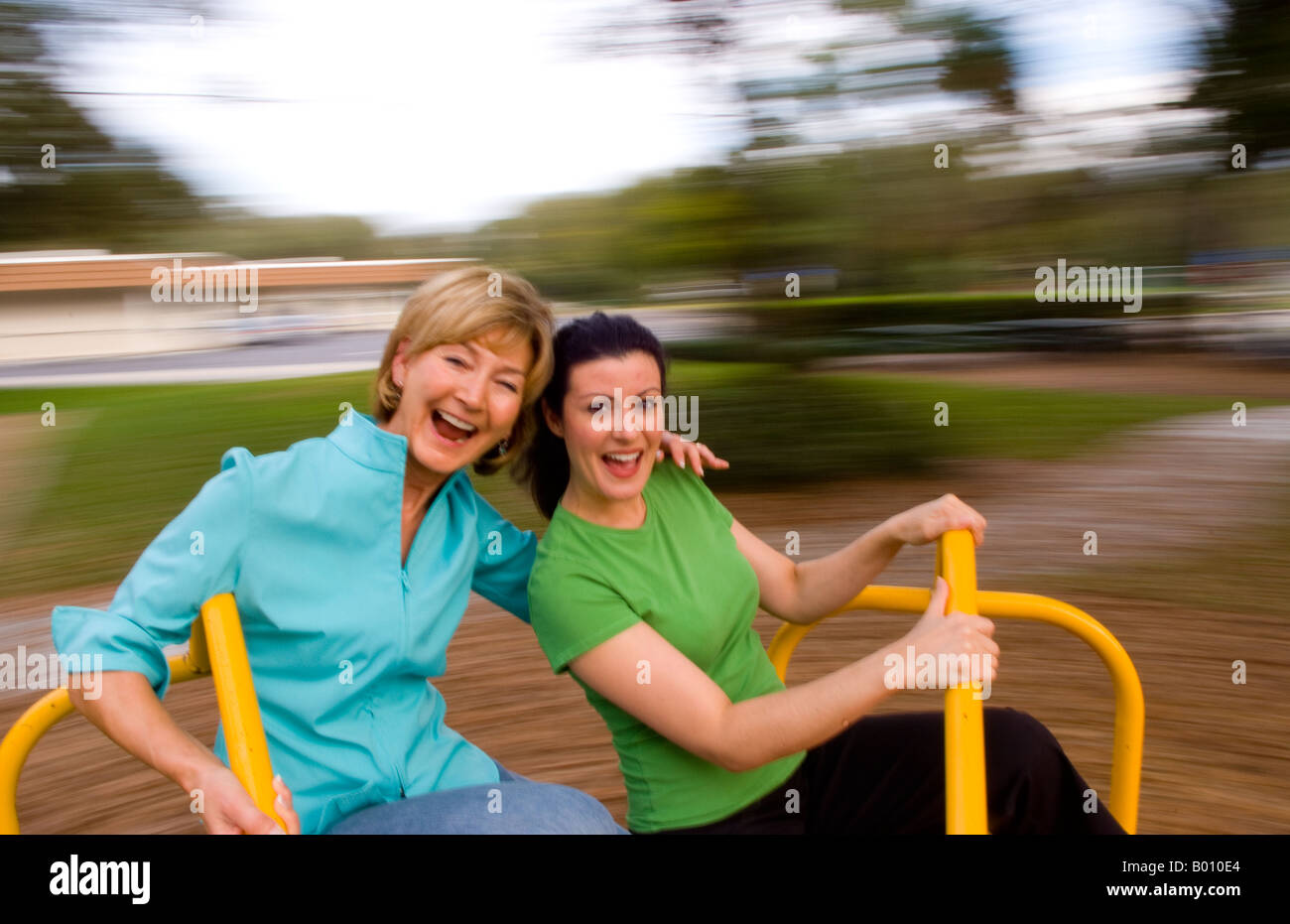 Mother and daughter or good friends having fun in playground spinning ...