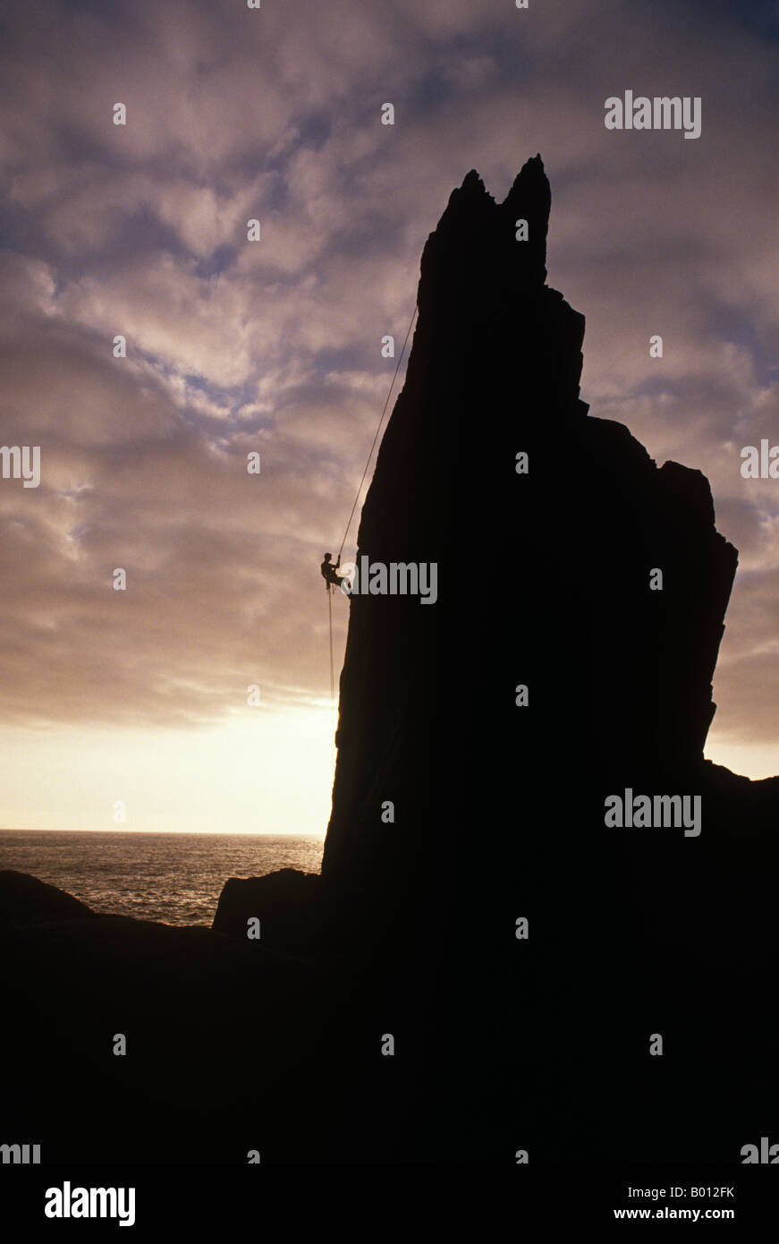 England, Devon, Lundy Island. Climber abseiling the Needle at dusk on ...