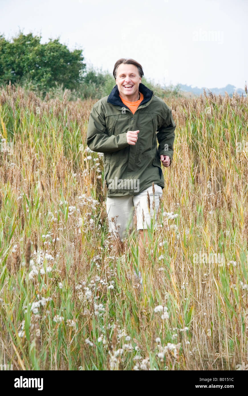 A happy smiling 43 year old man is jogging through tall grass on a ...