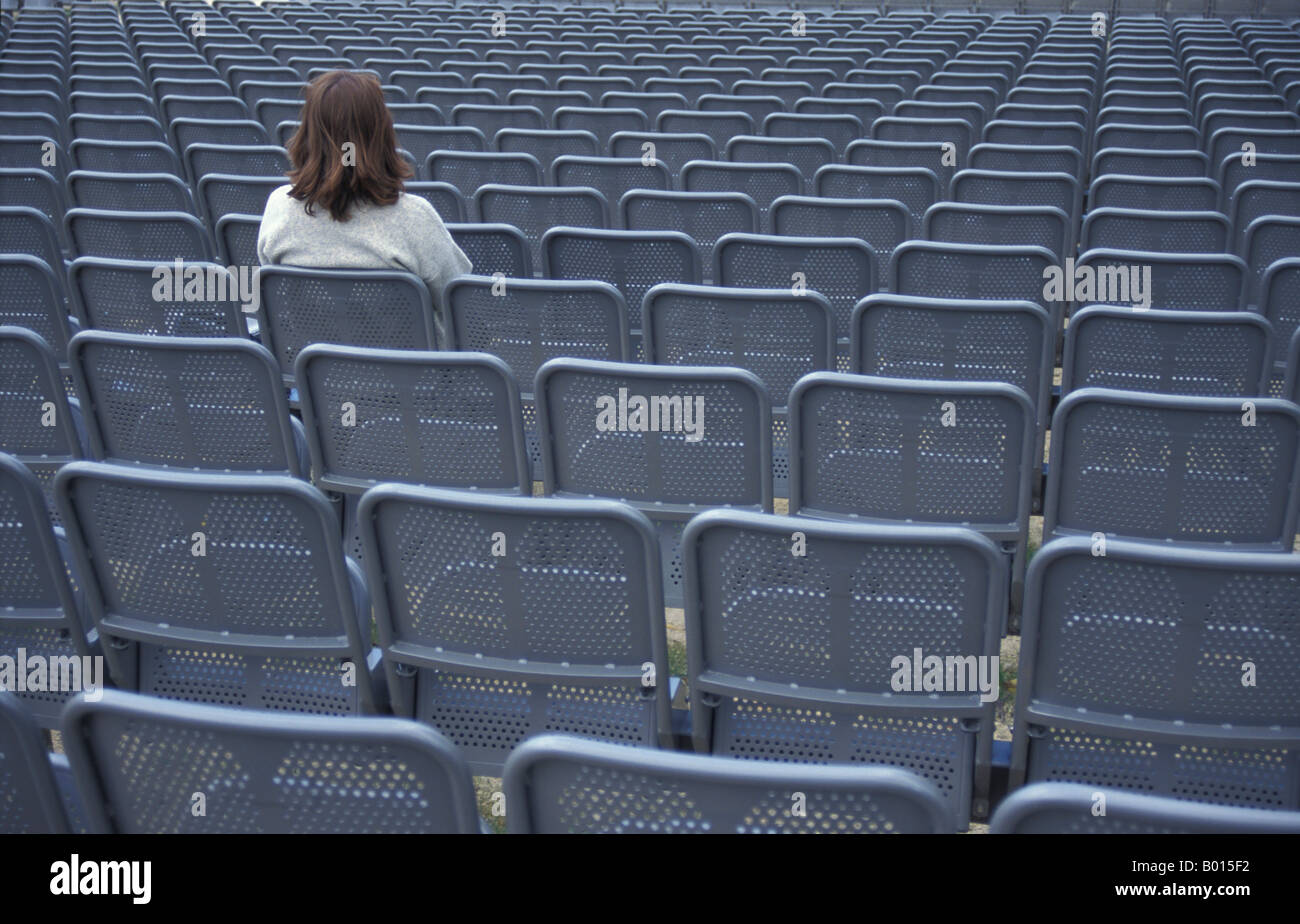 Woman sits alone in empty seat rows Stock Photo - Alamy