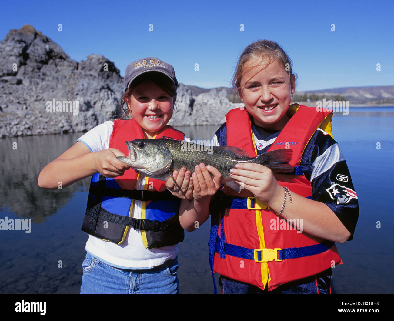 Two young girls hold a large largemouth bass they have just caught from ...