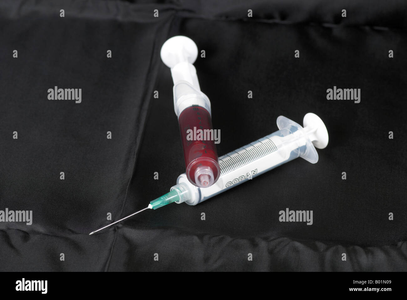 Blood in a syringe over a syringe with a needle attached but covered on ...