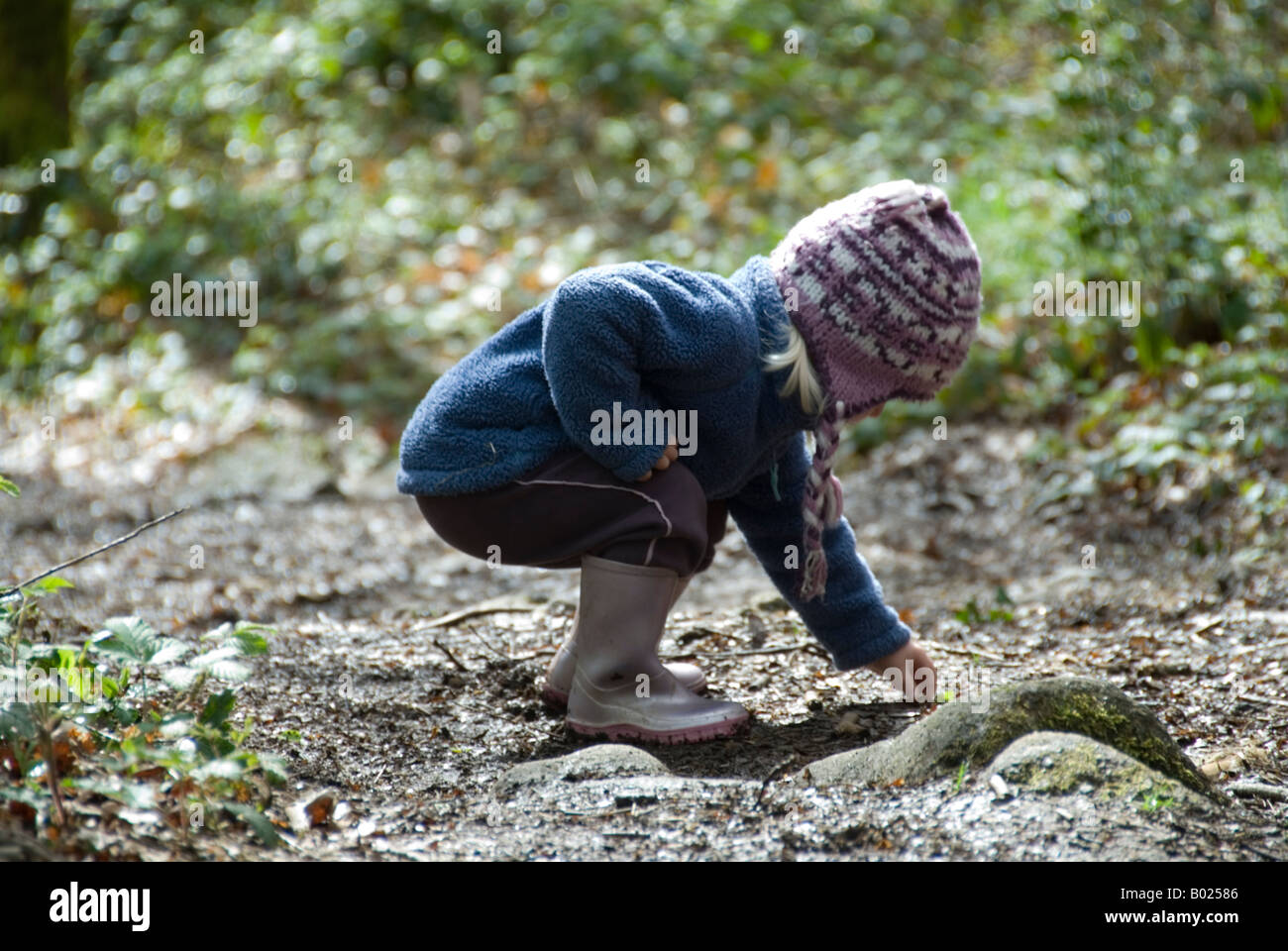 Stock photo of a two year old girl stooping to inspect an insect on a ...
