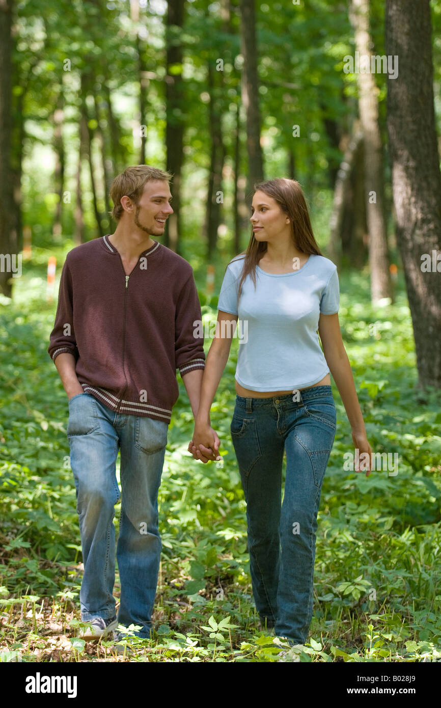full body portrait of young couple walking hand in hand through forest ...