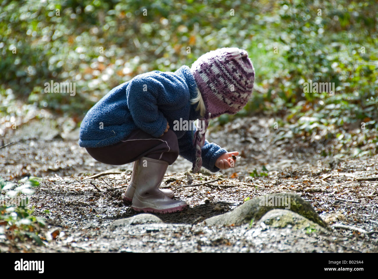 Stock photo of a two year old girl stooping to inspect an insect on a ...