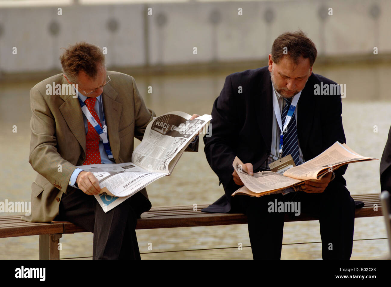 Two men reading newspapers on park bench Stock Photo - Alamy