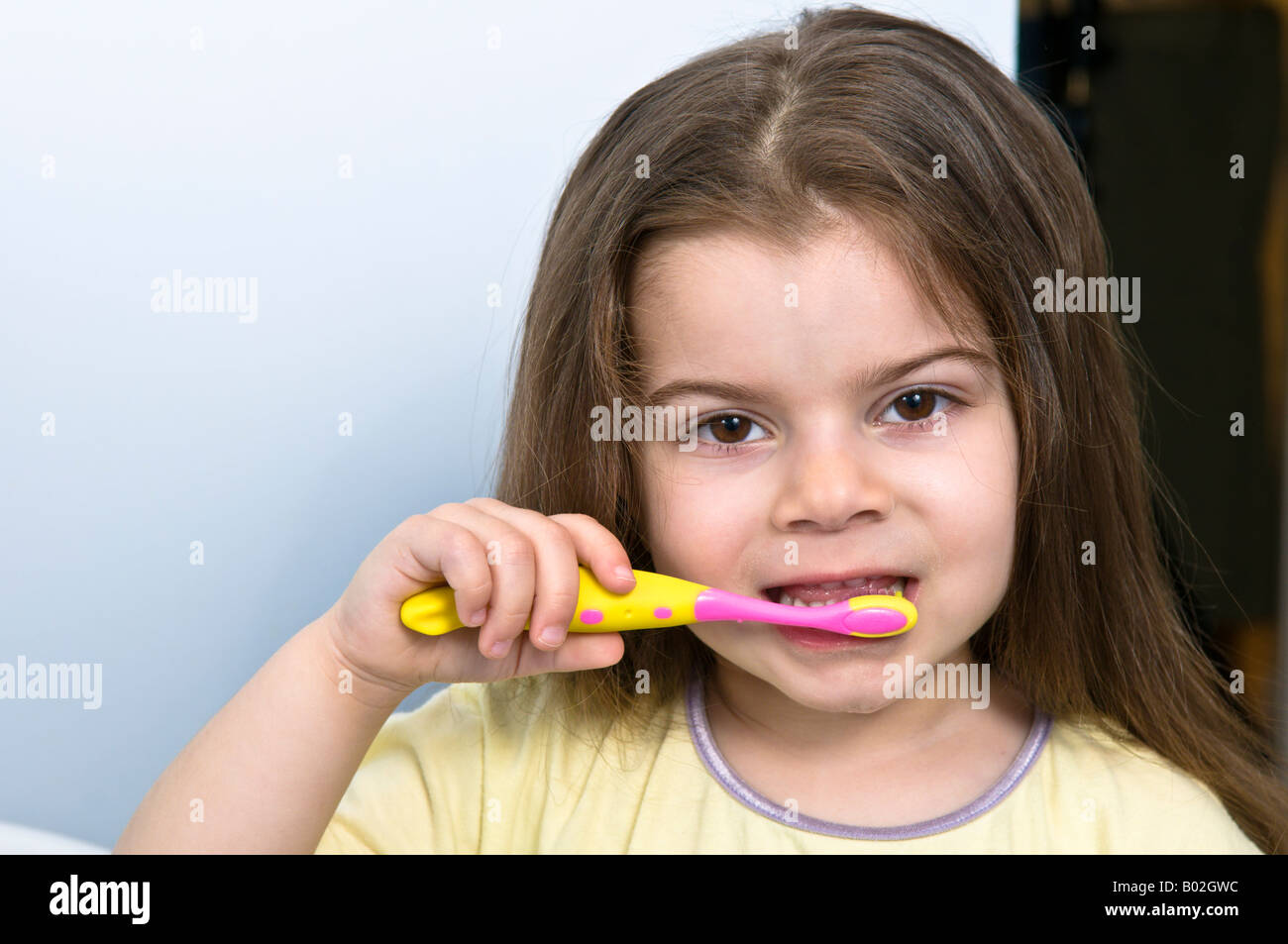 A young girl 4 years old with long brown hair brushes her teeth with a ...