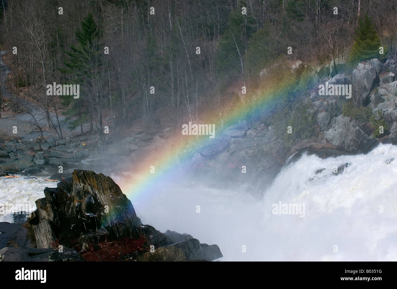 End of a waterfall with rainbow and rocks in the spray. Dark rocks in ...