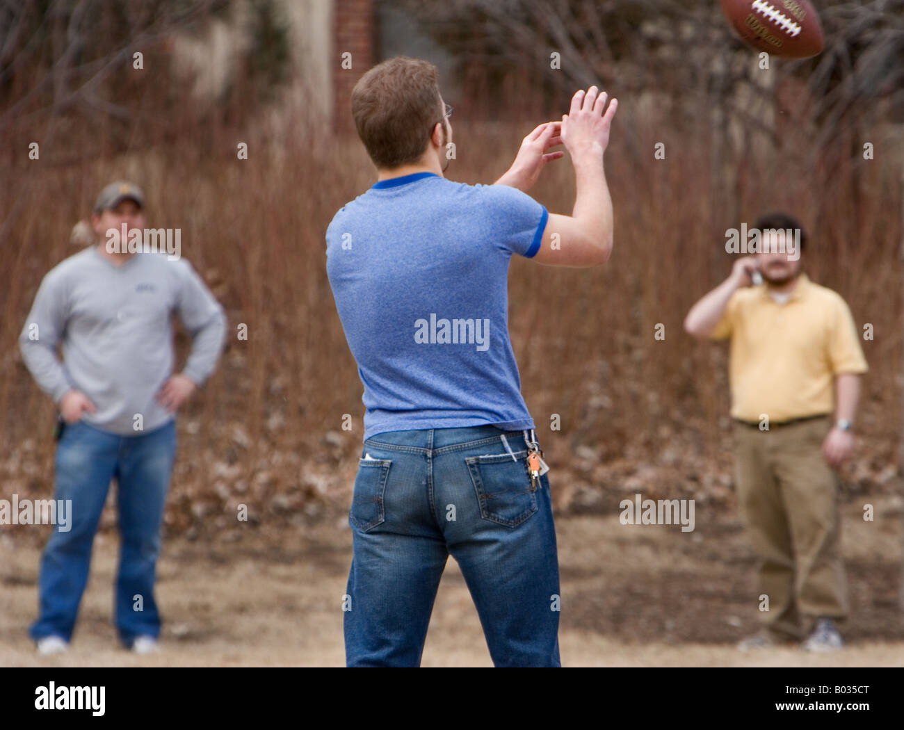 Three men throw an American football around on a college campus in ...