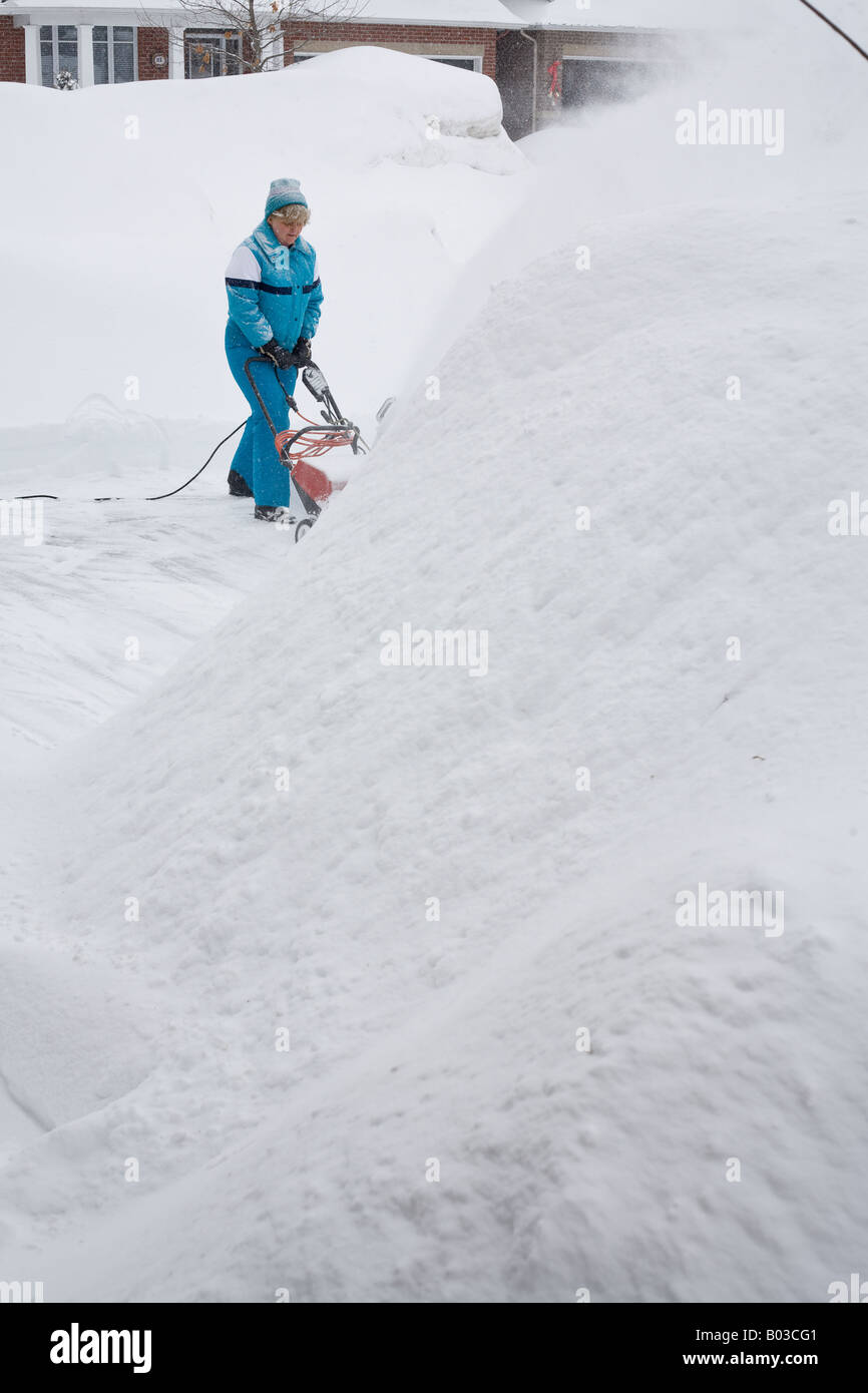 Woman with Electric Snowblower vertical A woman in a blue snowsuit uses ...