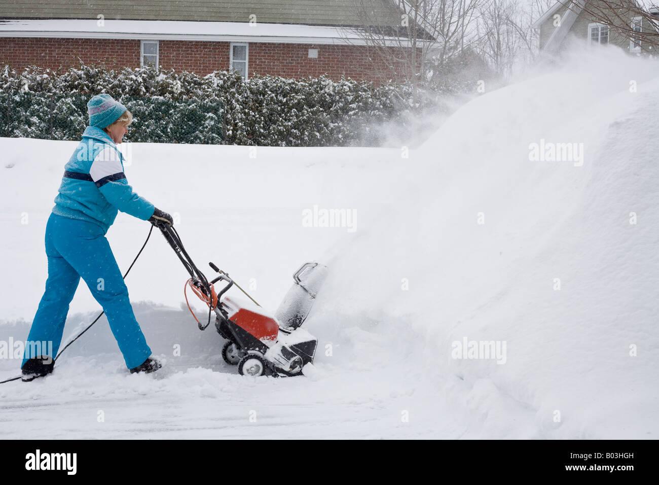 Woman pushing an Electric Snowblower A woman in a blue snow suit pushes ...