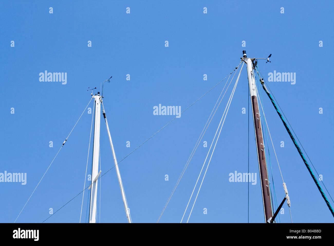 Two sailing ship masts anchored by wires against a bright blue sky ...