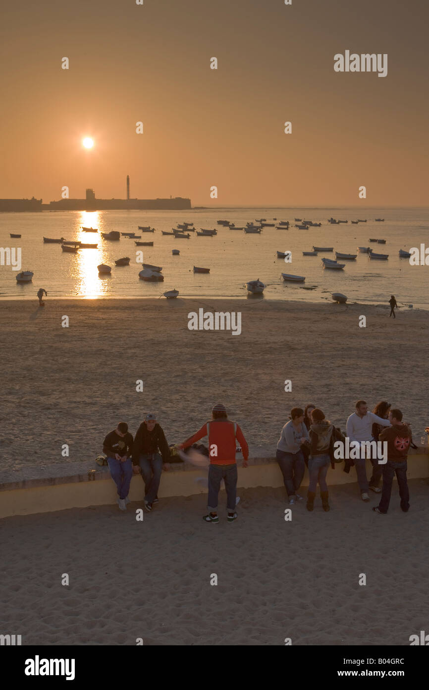 People gathered at Playa de la Caleta (beach) at sunset, backdropped by ...
