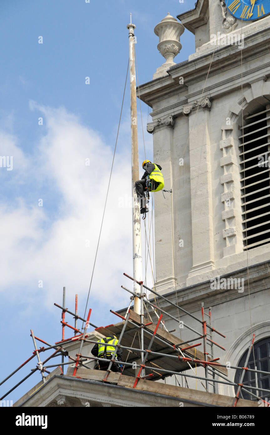 Workman suspended around flag pole carrying out maintenance work during ...