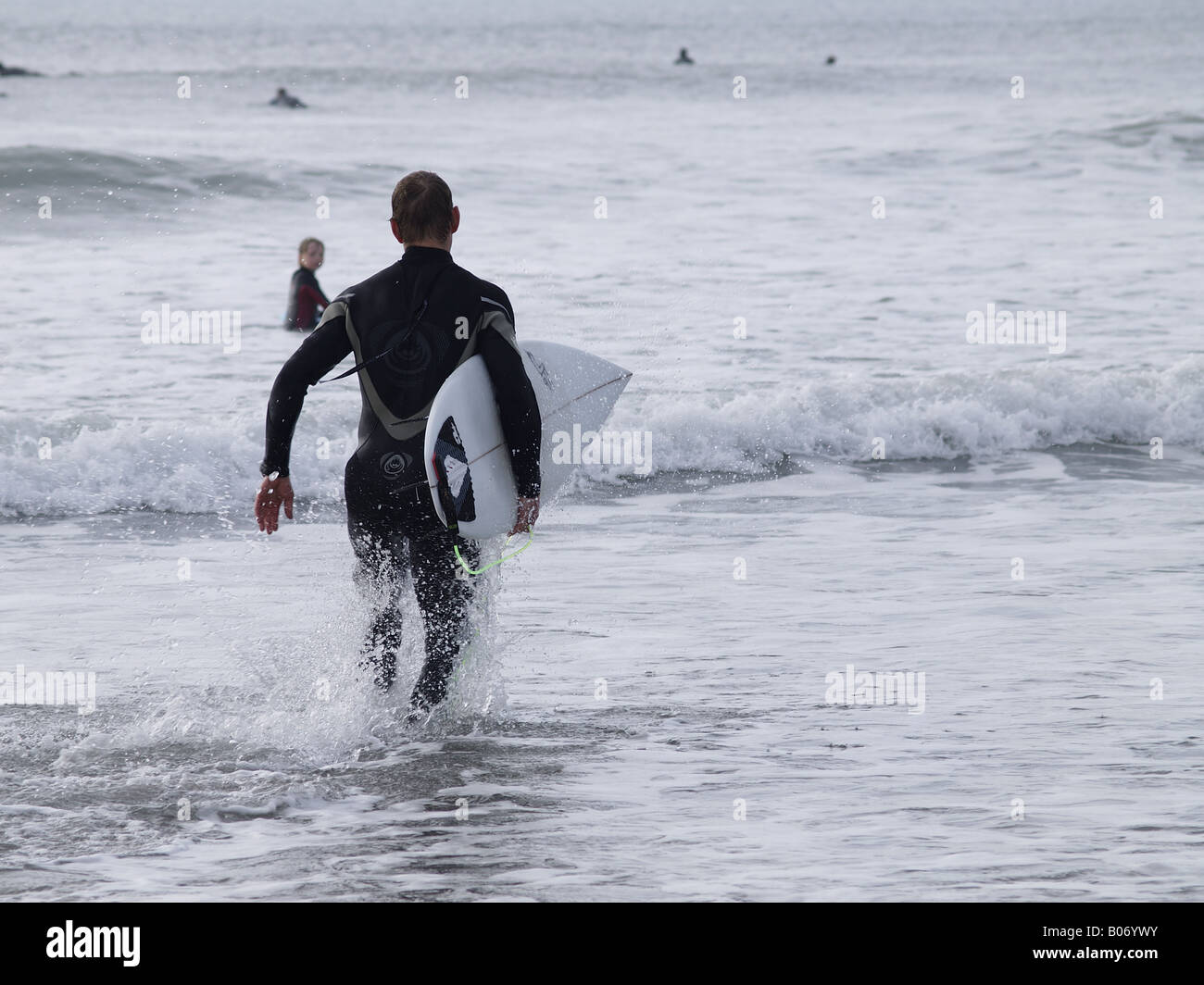 Surfer wearing a wetsuit and holding a surfboard under his arm, running ...