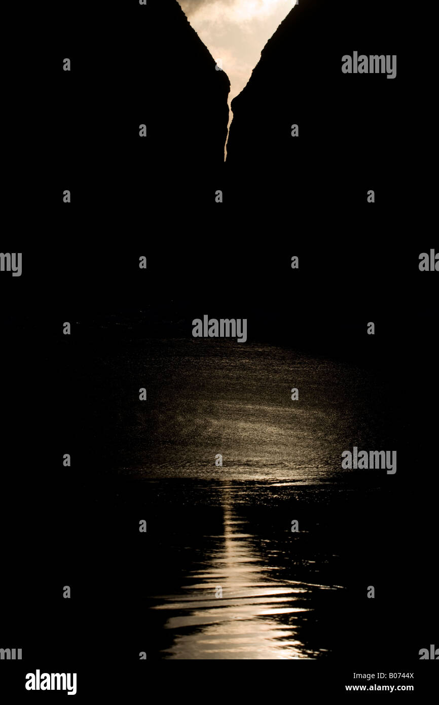 Sunset light filters through a slit between two sea stacks and ...