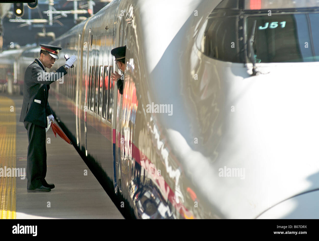 Platform guard saluting the driver conductor of a departing Shinkansen ...