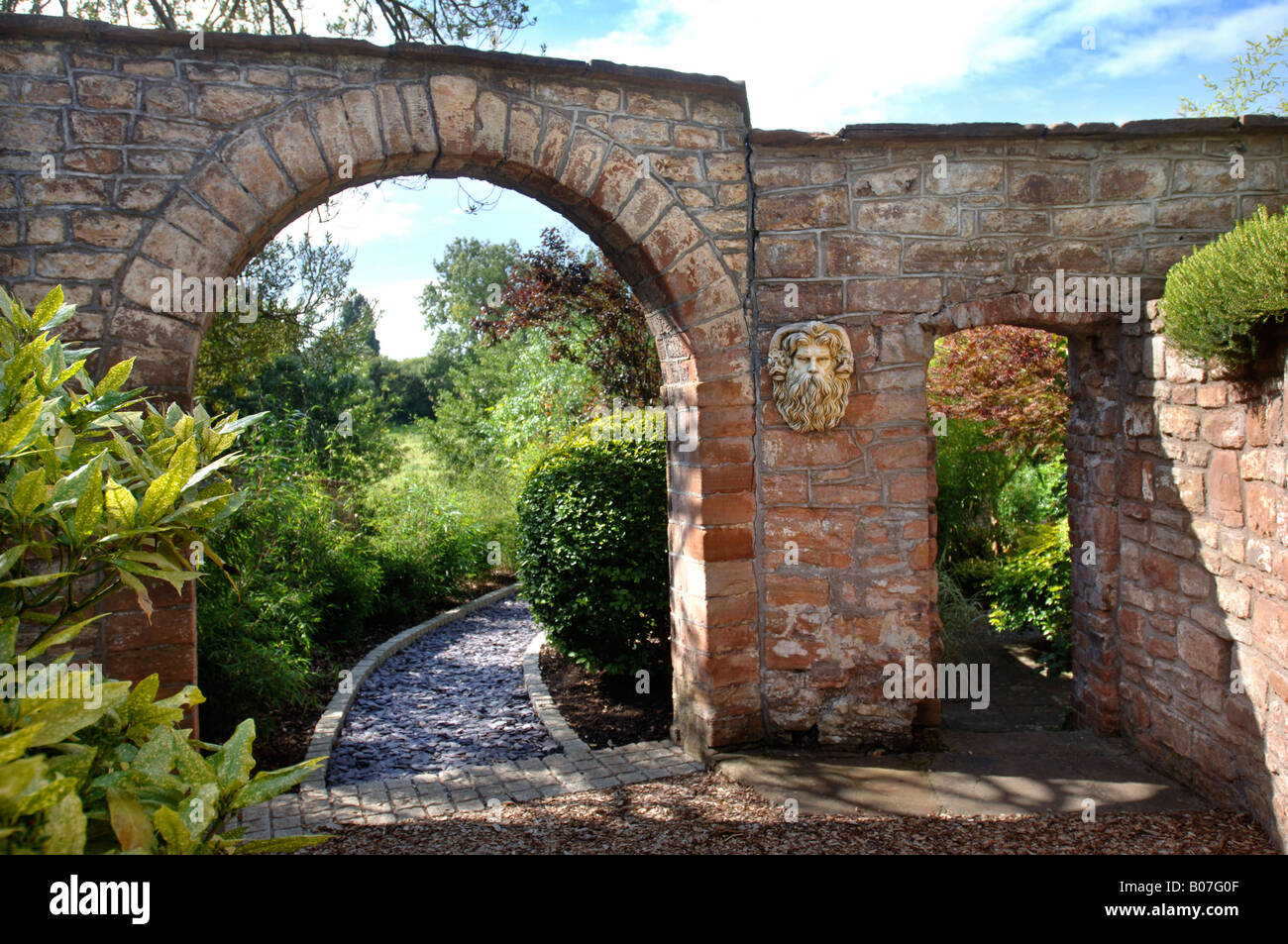 A STONE ARCH LEADING TO A GARDEN PATH LAYED WITH SLATE SHARDS AND EDGED ...