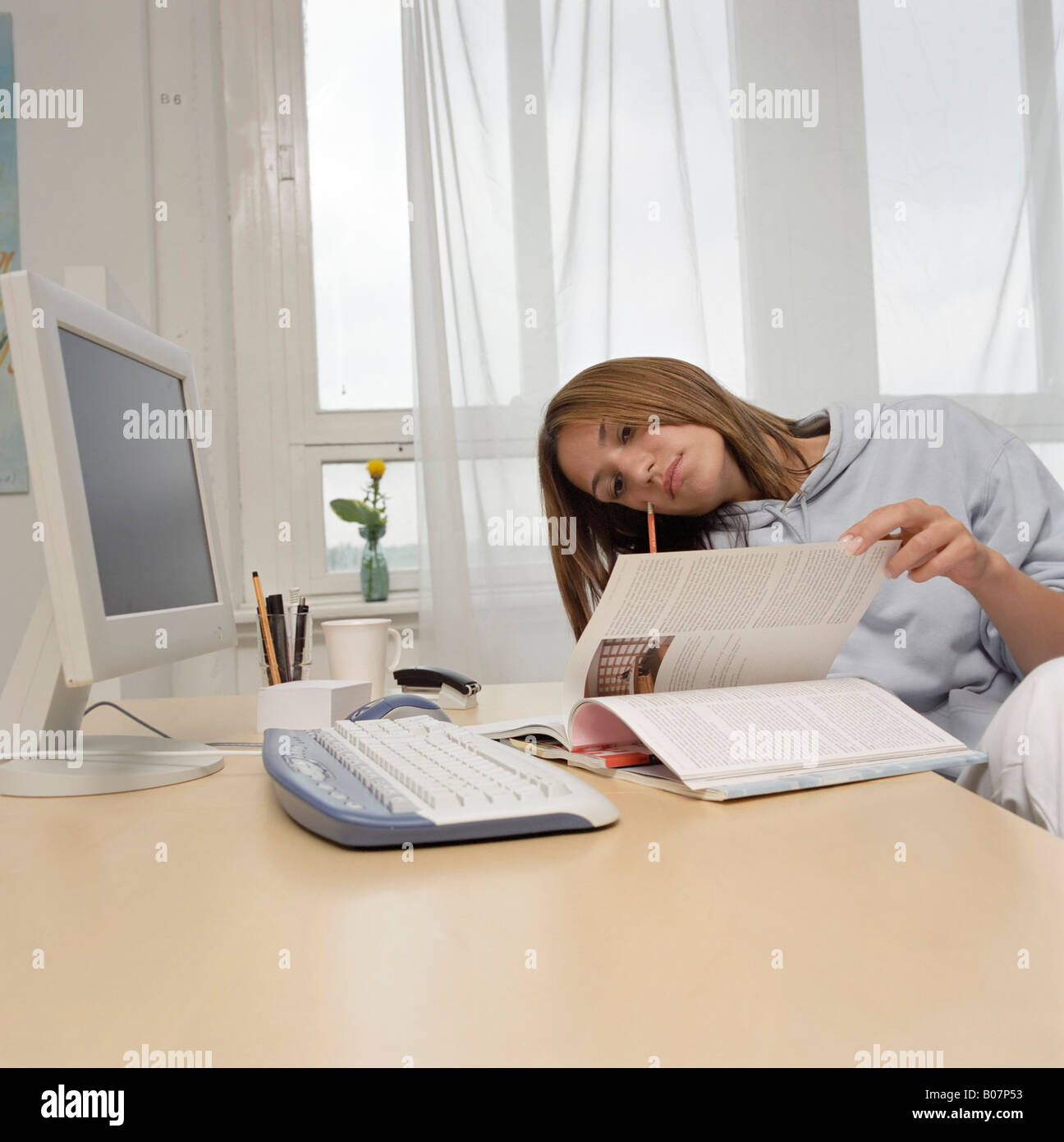 Young woman sitting in front of a computer while chewing on a pen Stock ...