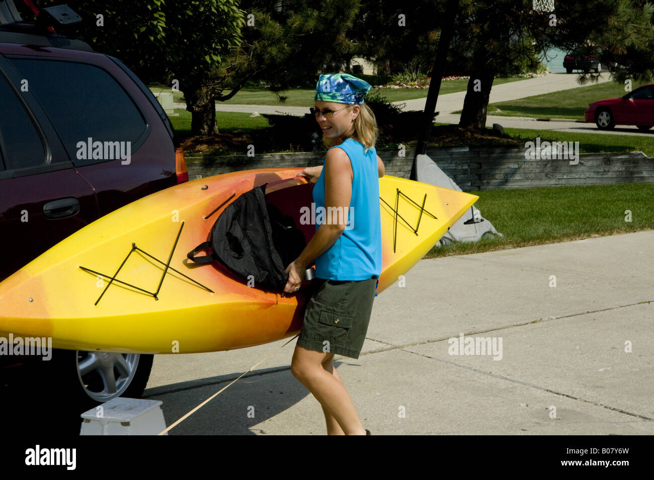 Woman carries kayak to SUV in driveway Stock Photo - Alamy