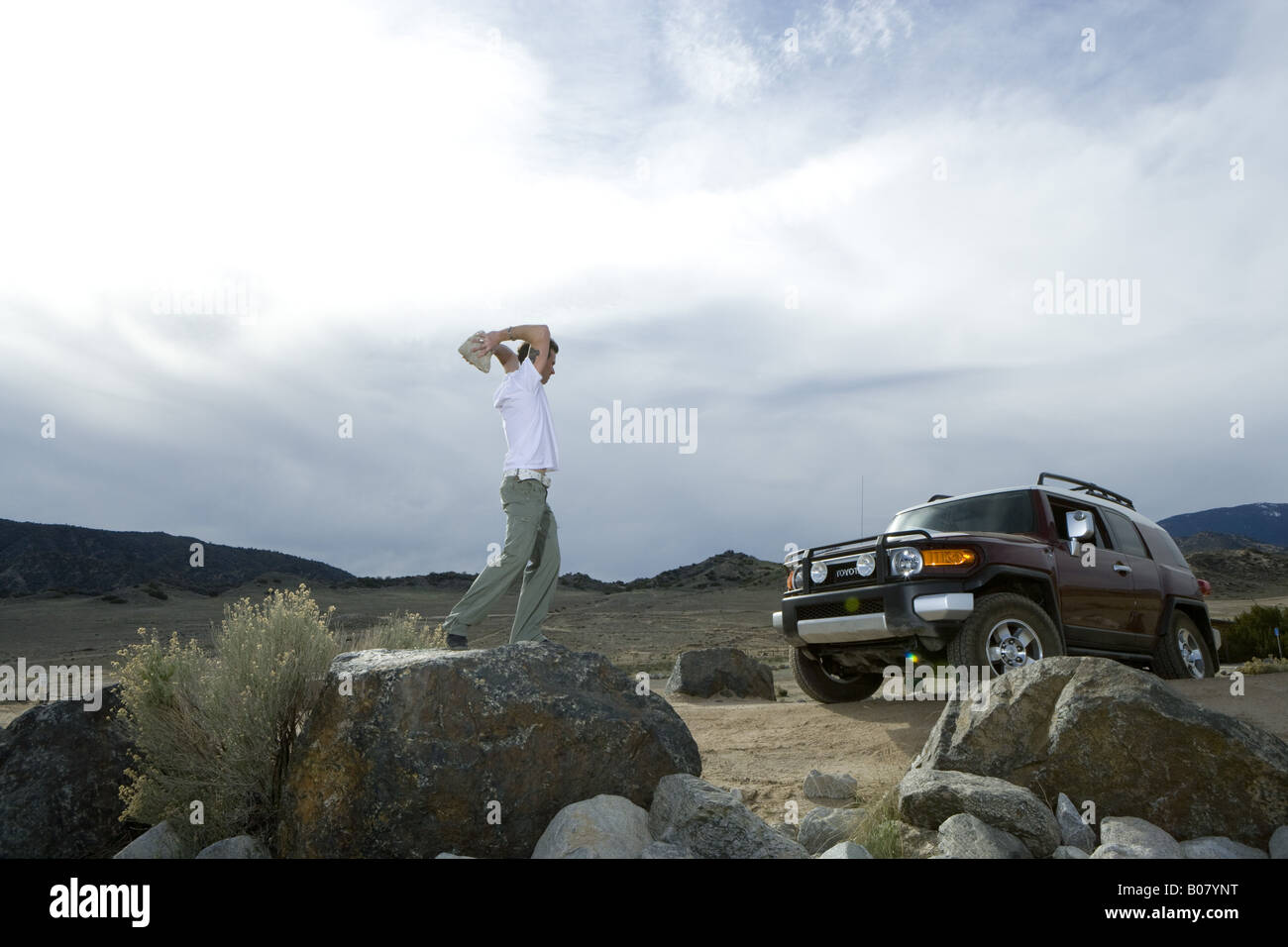 Man pretends to throw rock at SUV in desert Stock Photo - Alamy