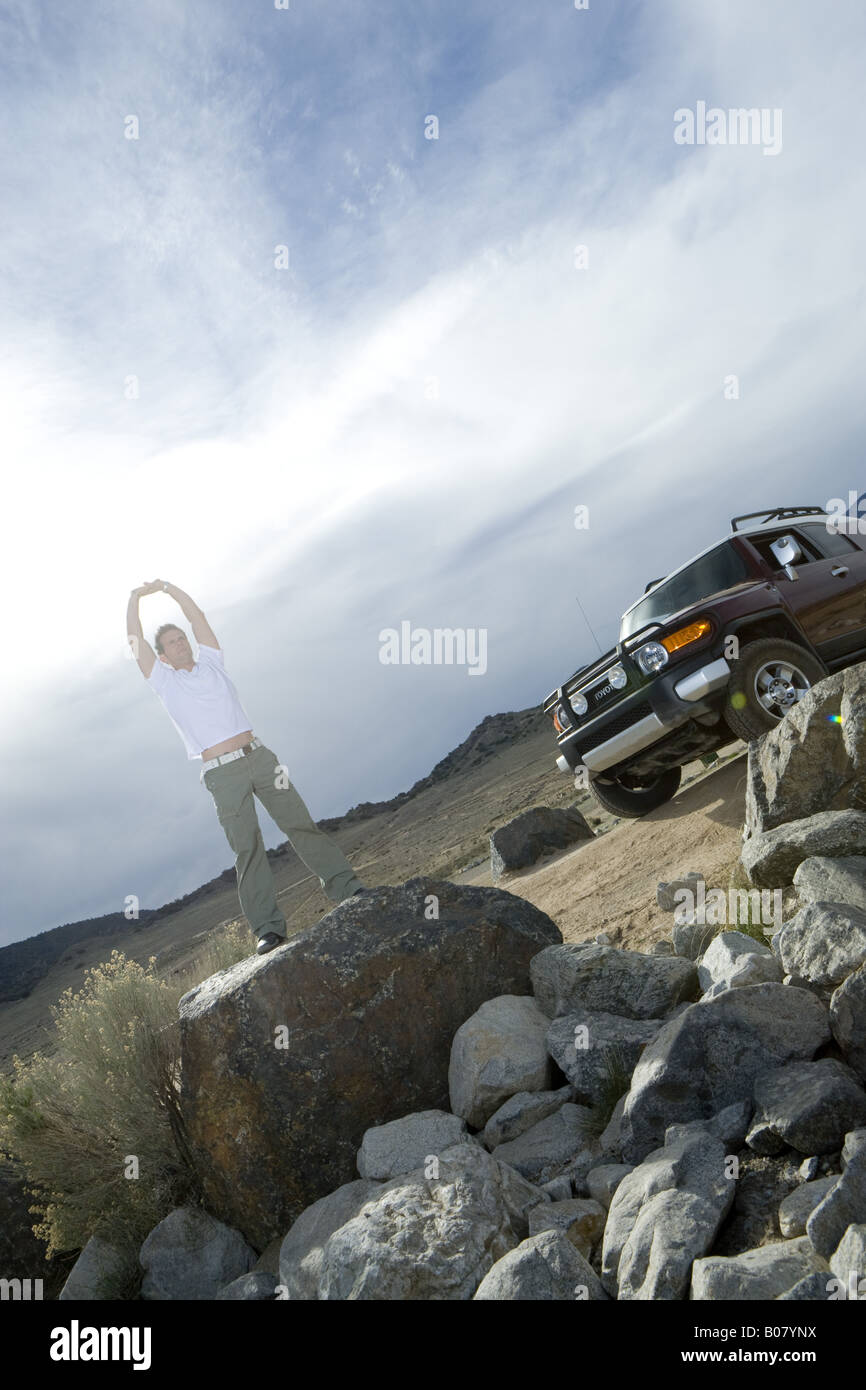 Man stretches arms atop large rock in desert Stock Photo - Alamy