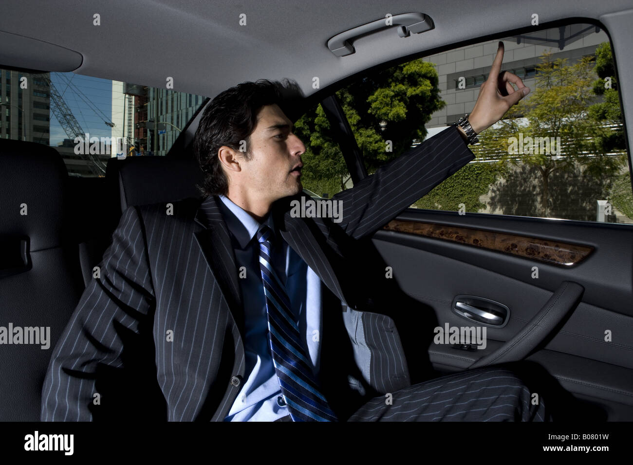 Asian business man seated in rear of car signalling through window ...