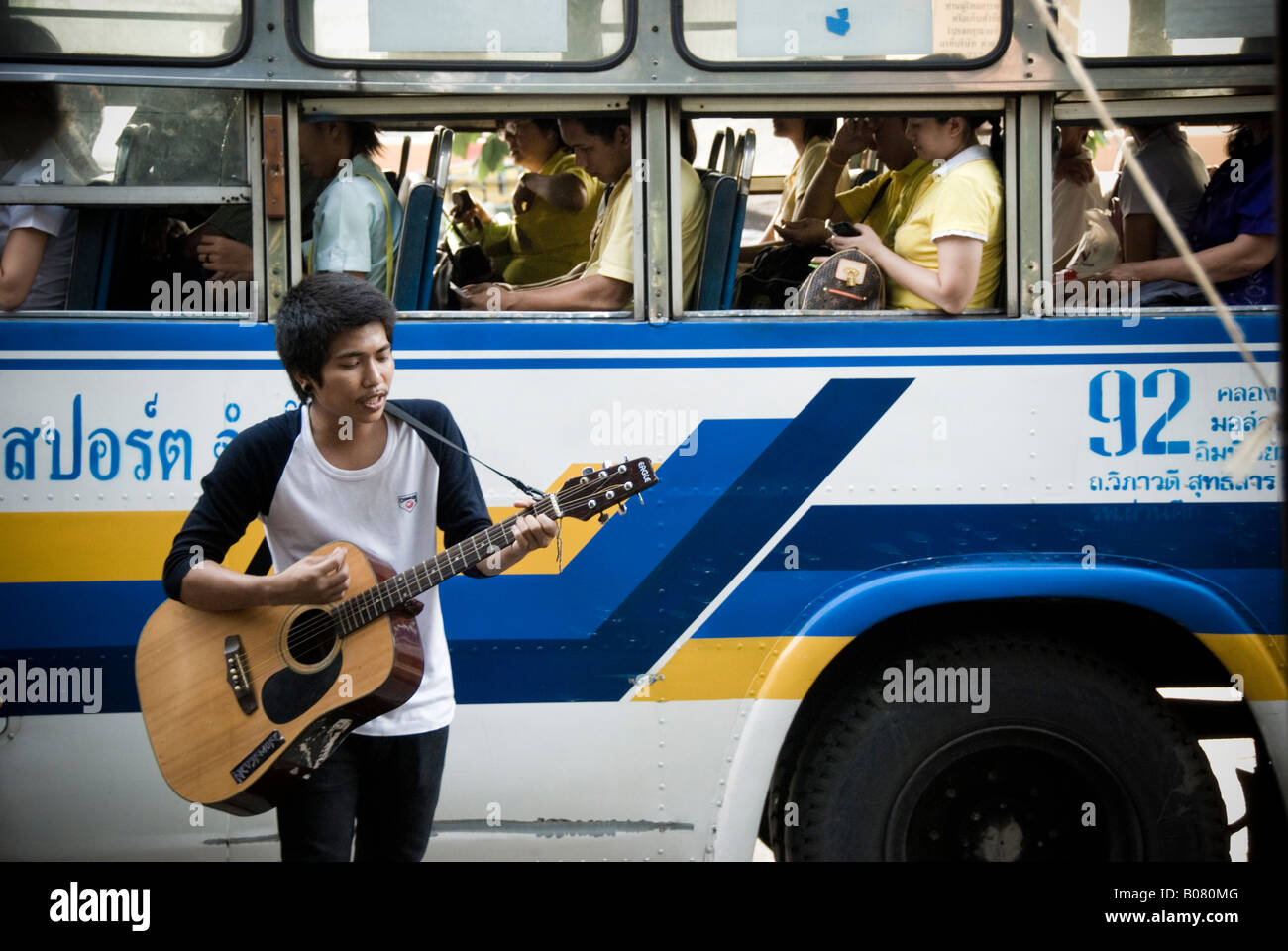 Young Asian man busking in city center. A bus drives by Stock Photo - Alamy