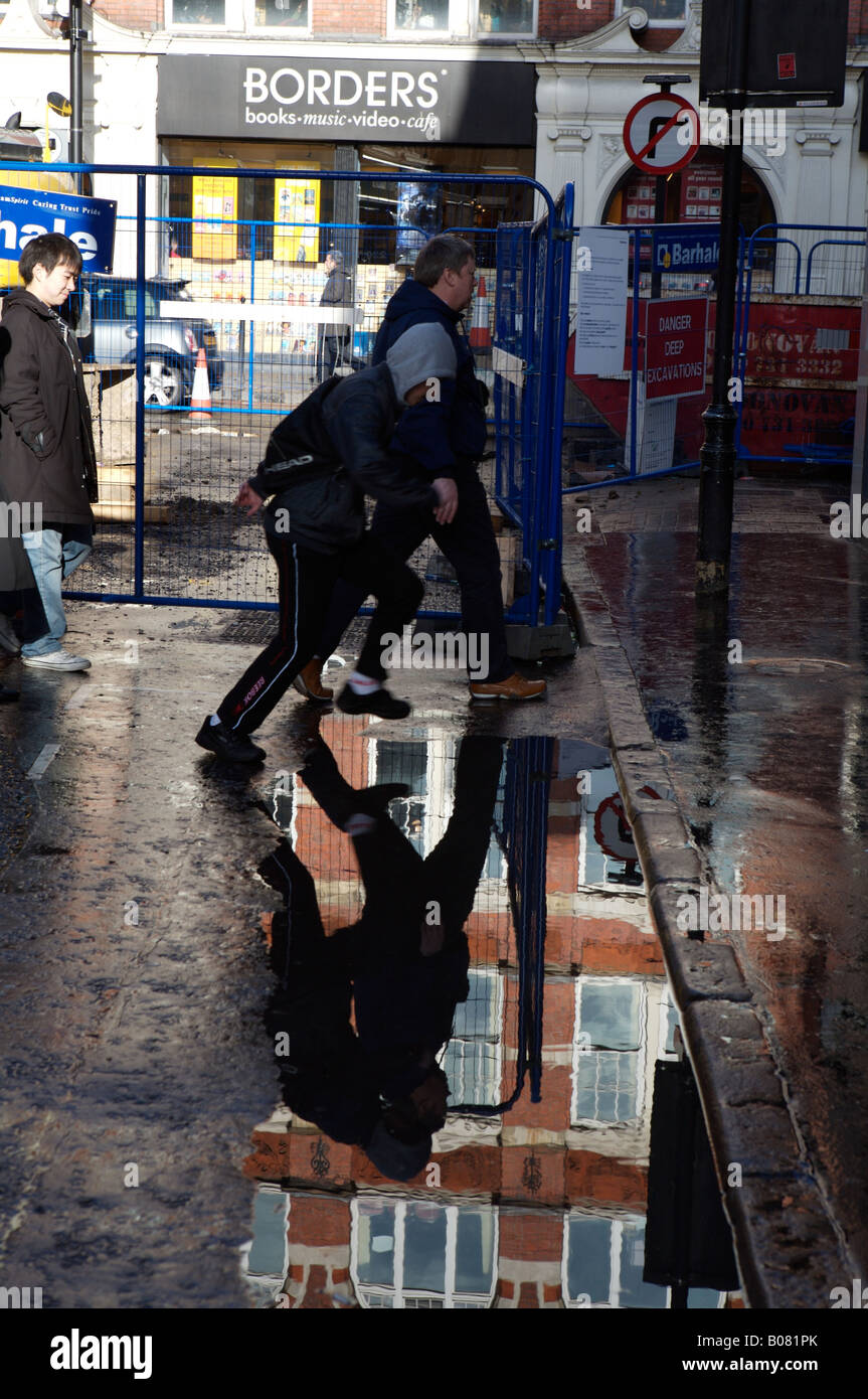 a street scene in london with a pedestrian jumping over a deep puddle ...