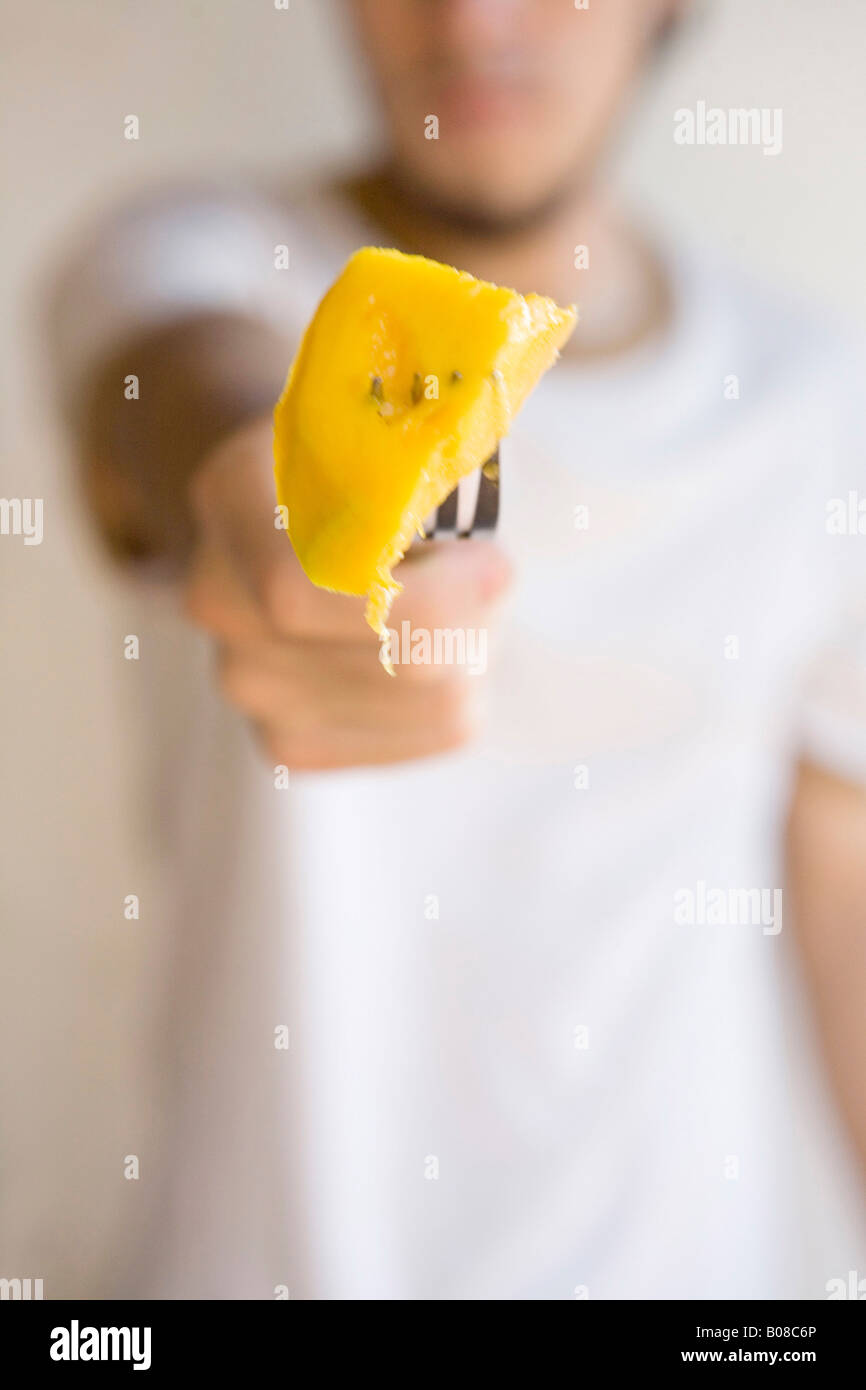 Man holding piece of mango on a fork Stock Photo - Alamy