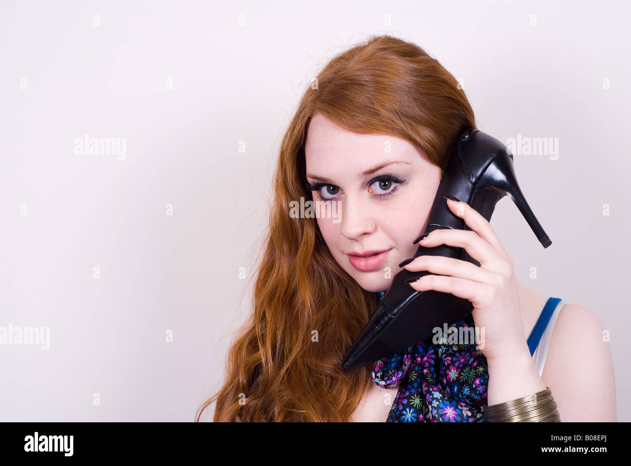 Beautiful redheaded woman holding shoe next to ear Stock Photo - Alamy